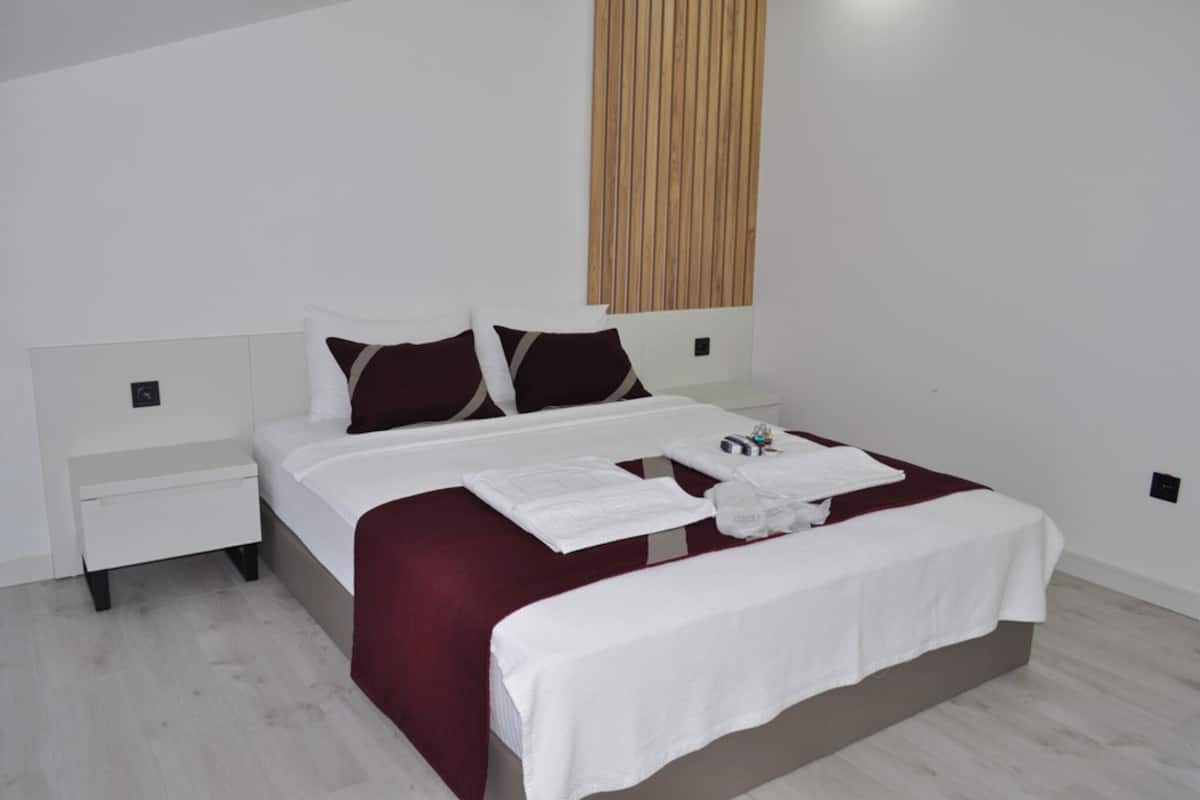 Quarto moderno com cama, mesinhas de cabeceira brancas e painel de parede de madeira.