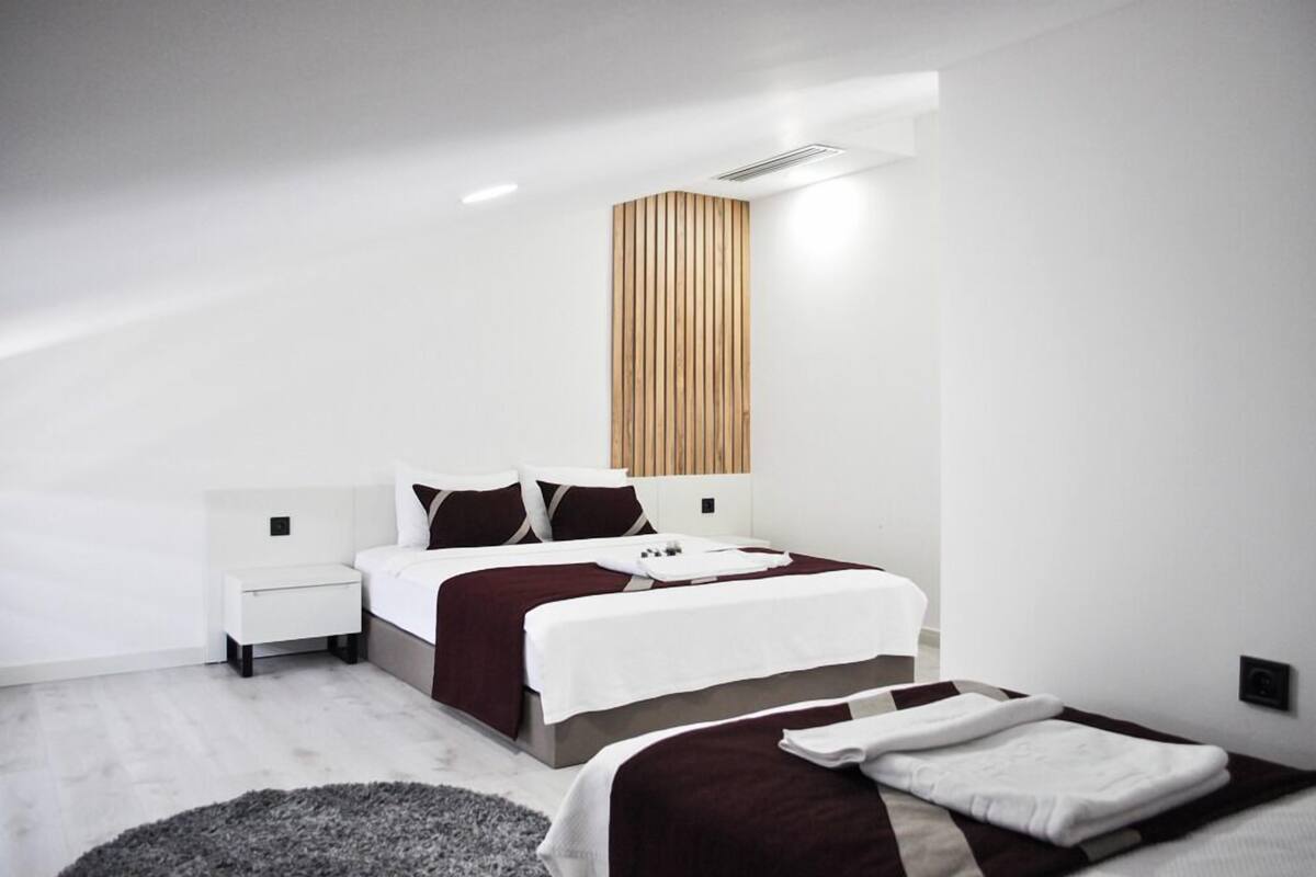 Um quarto moderno com uma cama grande, uma mesinha de cabeceira, uma parede de destaque em madeira e um tapete cinza.