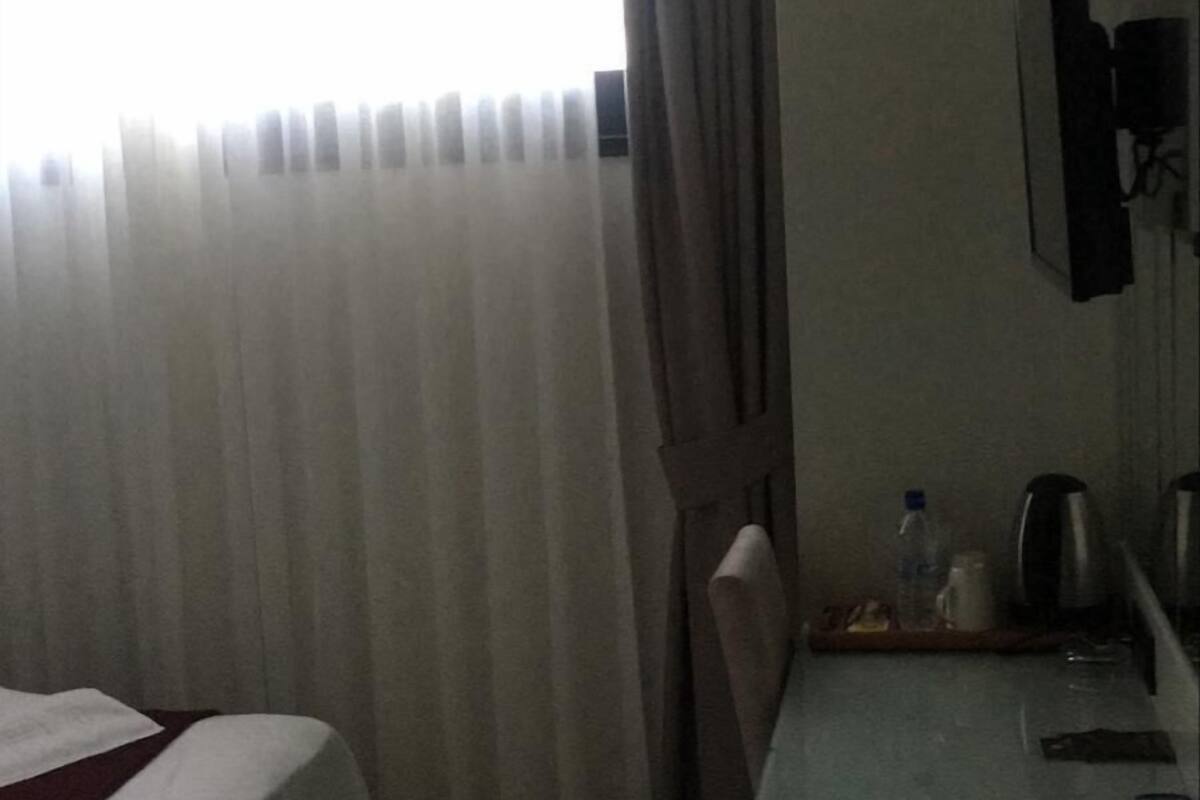 Quarto de hotel com uma cama, uma mesa, uma cadeira, uma televisão e uma janela com cortinas.