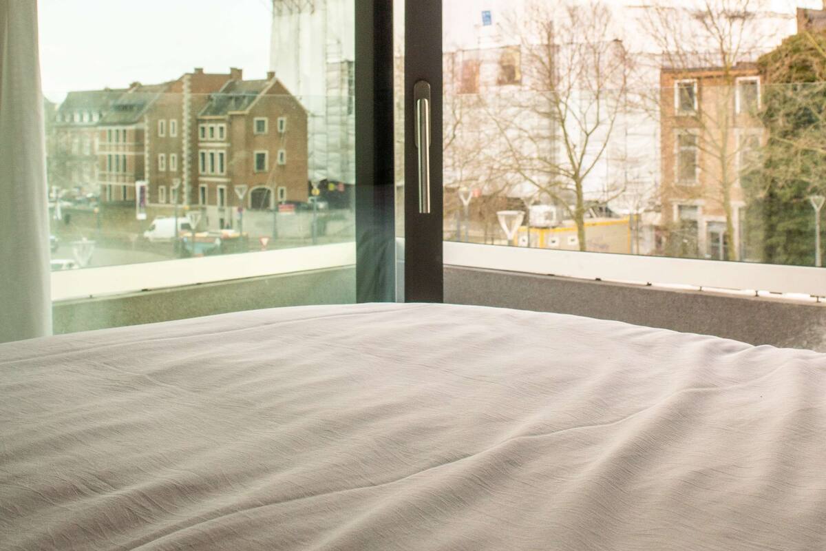 Quarto com uma janela grande, uma cama e vista para edifícios.