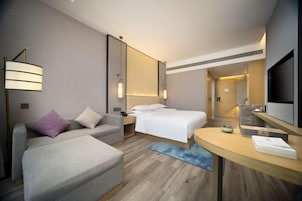 Quarto de hotel moderno com cama, sofá, escrivaninha e televisão.