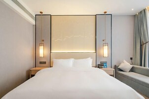 Quarto de hotel com uma cama grande, mesas de cabeceira, um sofá e iluminação embutida na parede.