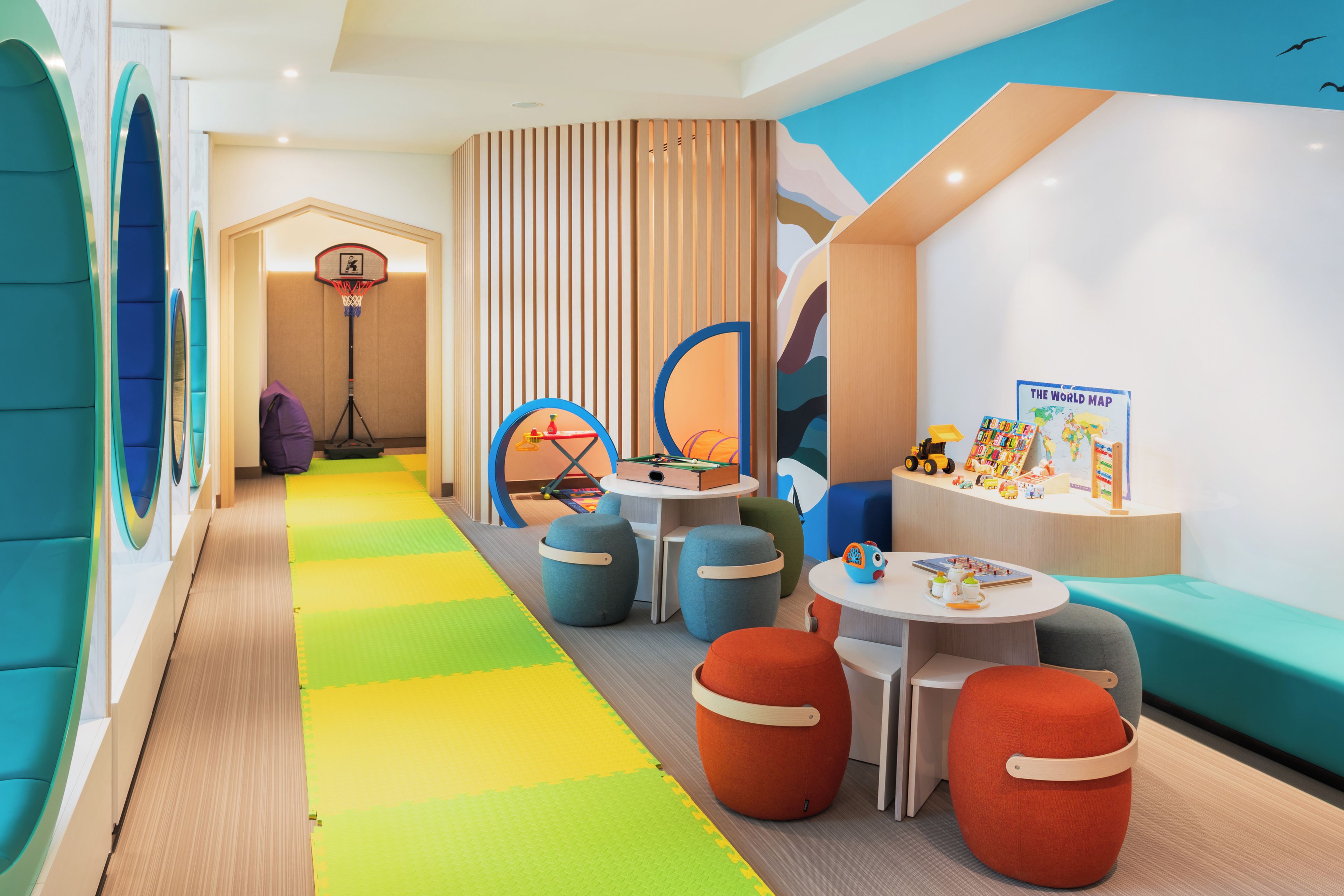 Uma área de recreação infantil com assentos coloridos, uma cesta de basquete e brinquedos educativos.