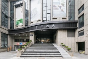 Entrada de hotel com design moderno, apresentando uma escadaria que leva à entrada e uma placa de identificação acima.