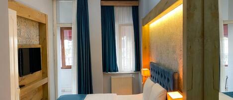 Quarto de hotel com cama, televisão, janela com cortinas e cabeceira com luz.
