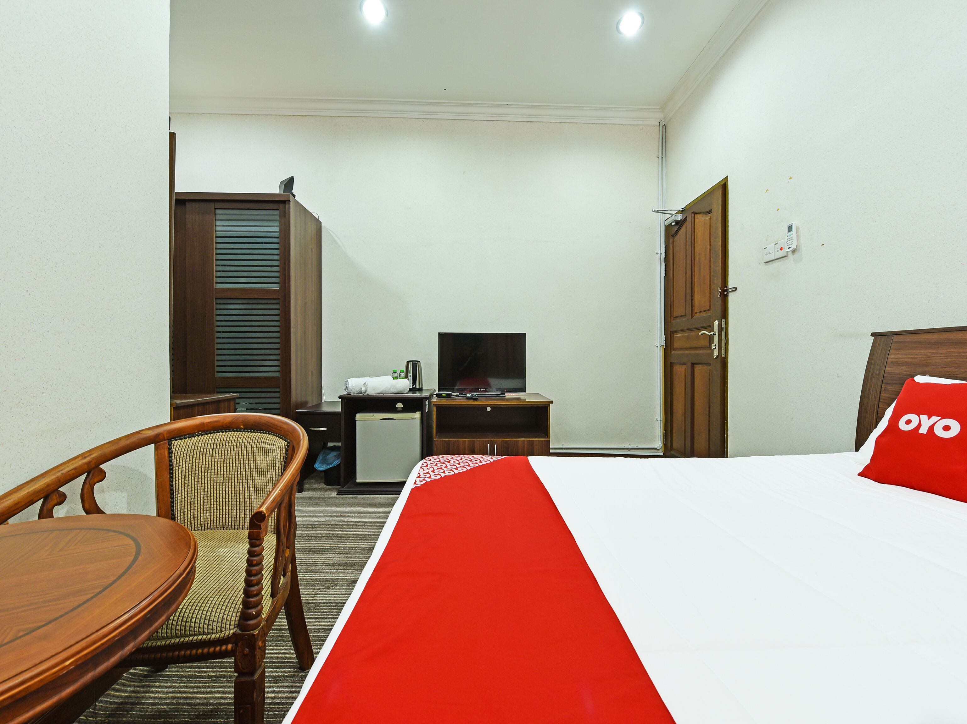 Quarto de hotel com cama, secretária, televisão, guarda-roupa e uma cadeira.