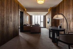 Quarto de hotel com decoração em madeira, um sofá, uma mesa redonda e uma luminária.