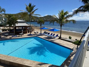 Piscina com espreguiçadeiras e guarda-sóis, área de bar e vista para a praia e oceano.