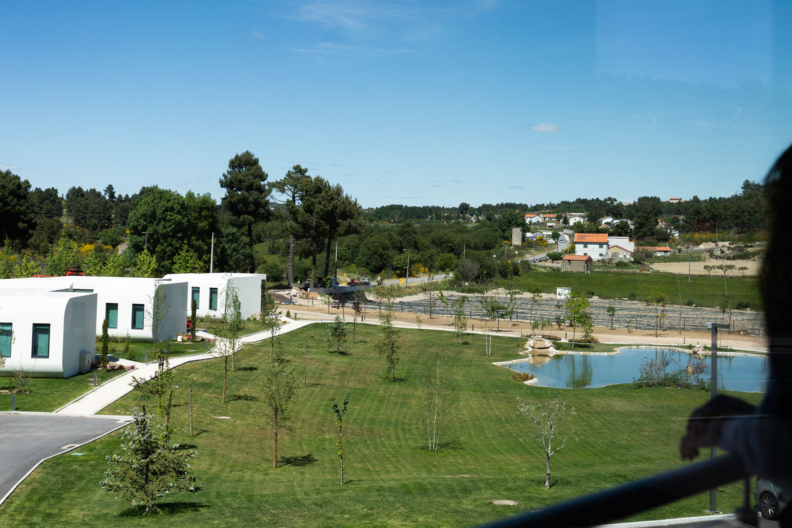 Um edifício moderno com fachada curva, um pequeno lago e um gramado bem cuidado.