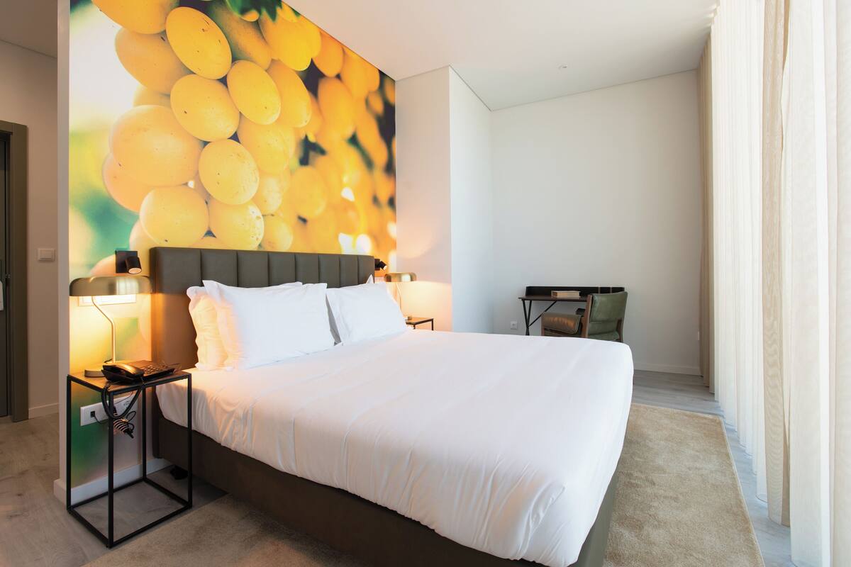 Quarto de hotel com uma cama grande, uma escrivaninha e um mural de frutas na parede.