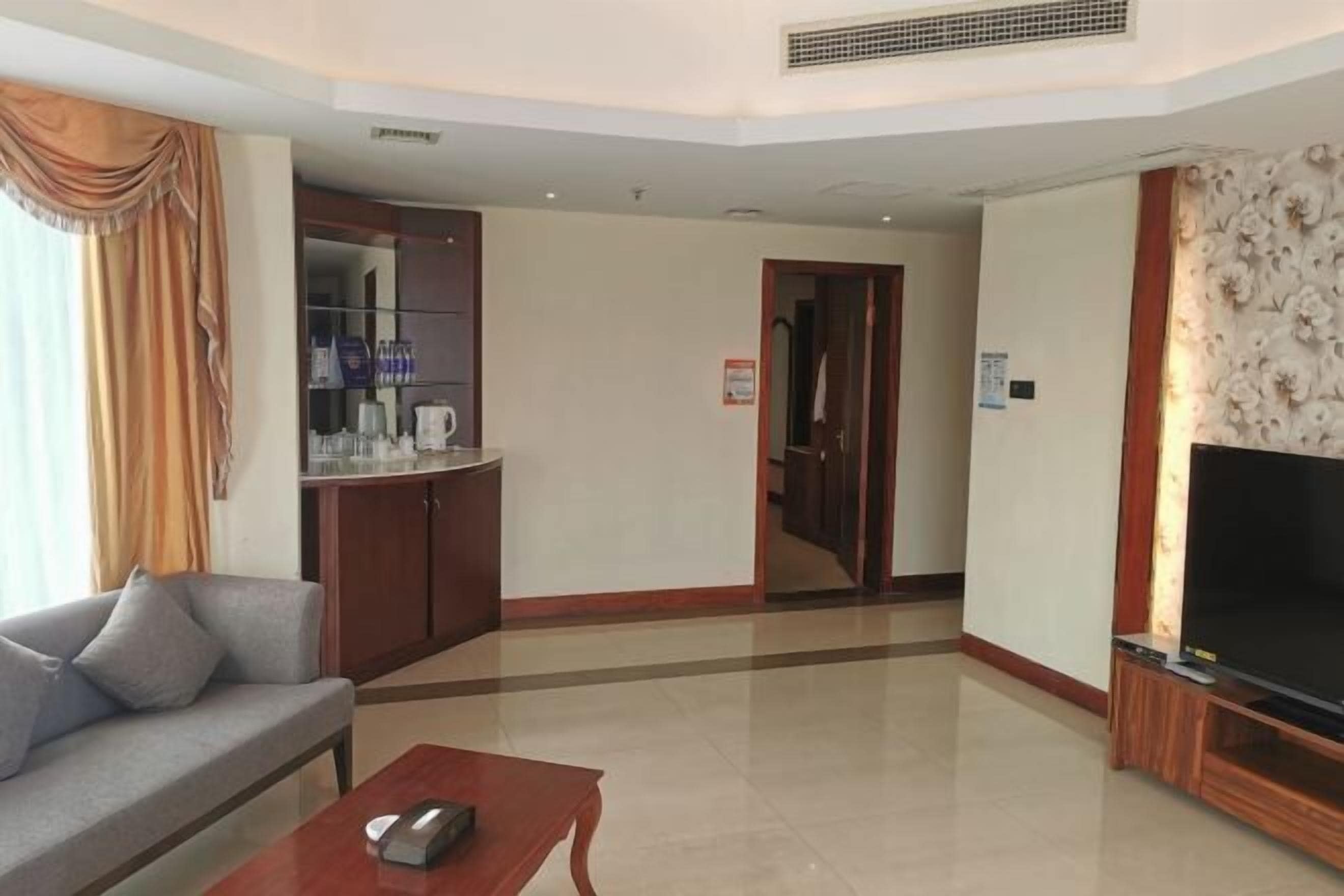 Quarto de hotel com sofá, mesa de centro, televisão, área de cozinha e banheiro.