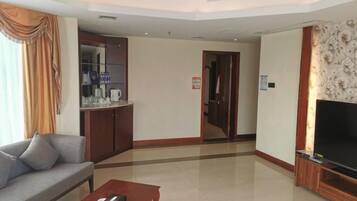 Quarto de hotel com sofá, mesa de centro, televisão, área de cozinha e banheiro.