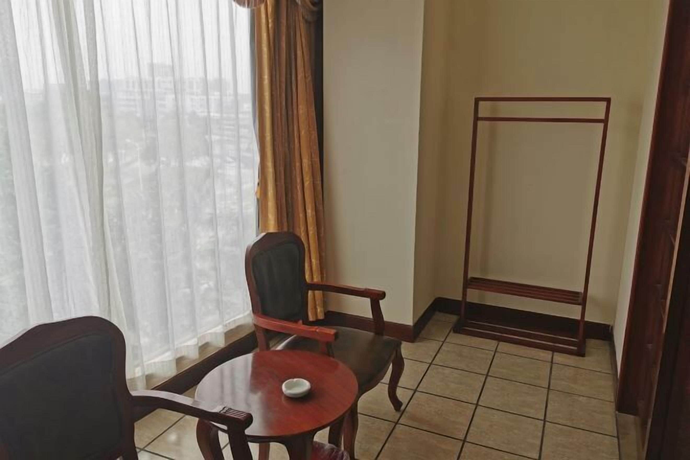Quarto de hotel com uma cadeira de madeira, uma mesa redonda pequena e um suporte de metal.