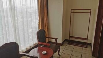 Quarto de hotel com uma cadeira de madeira, uma mesa redonda pequena e um suporte de metal.