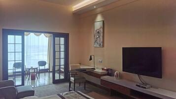 Quarto de hotel com cama, escrivaninha, cadeira, televisão e uma grande janela com cortinas.