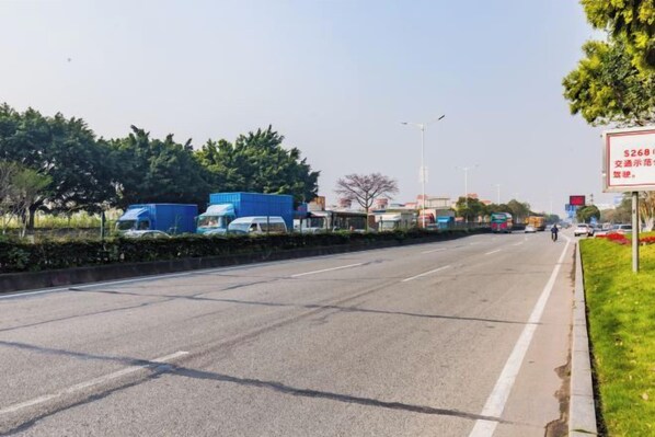 Uma estrada larga com veículos, um edifício azul e uma placa à direita.