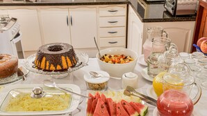 Uma mesa de buffet com diversos pratos, incluindo um bolo bundt de chocolate, salada de frutas, ovos mexidos e fatias de melancia.