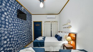 Quarto de hotel com duas camas, uma televisão, um abajur e uma porta com padrão decorativo.