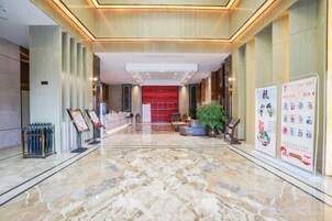 Um hall de hotel com piso de mármore, balcão de recepção e parede vermelha ao fundo.