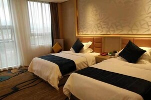 Quarto de hotel com duas camas, uma janela grande com cortinas leves, parede estampada e piso de madeira.
