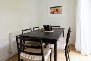 Uma mesa de jantar com seis cadeiras, um jogo americano tecido e uma moldura com uma imagem na parede.