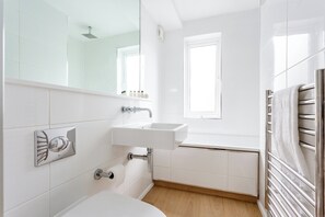 Uma casa de banho moderna com uma pia branca, um espelho, um chuveiro e um porta-toalhas.
