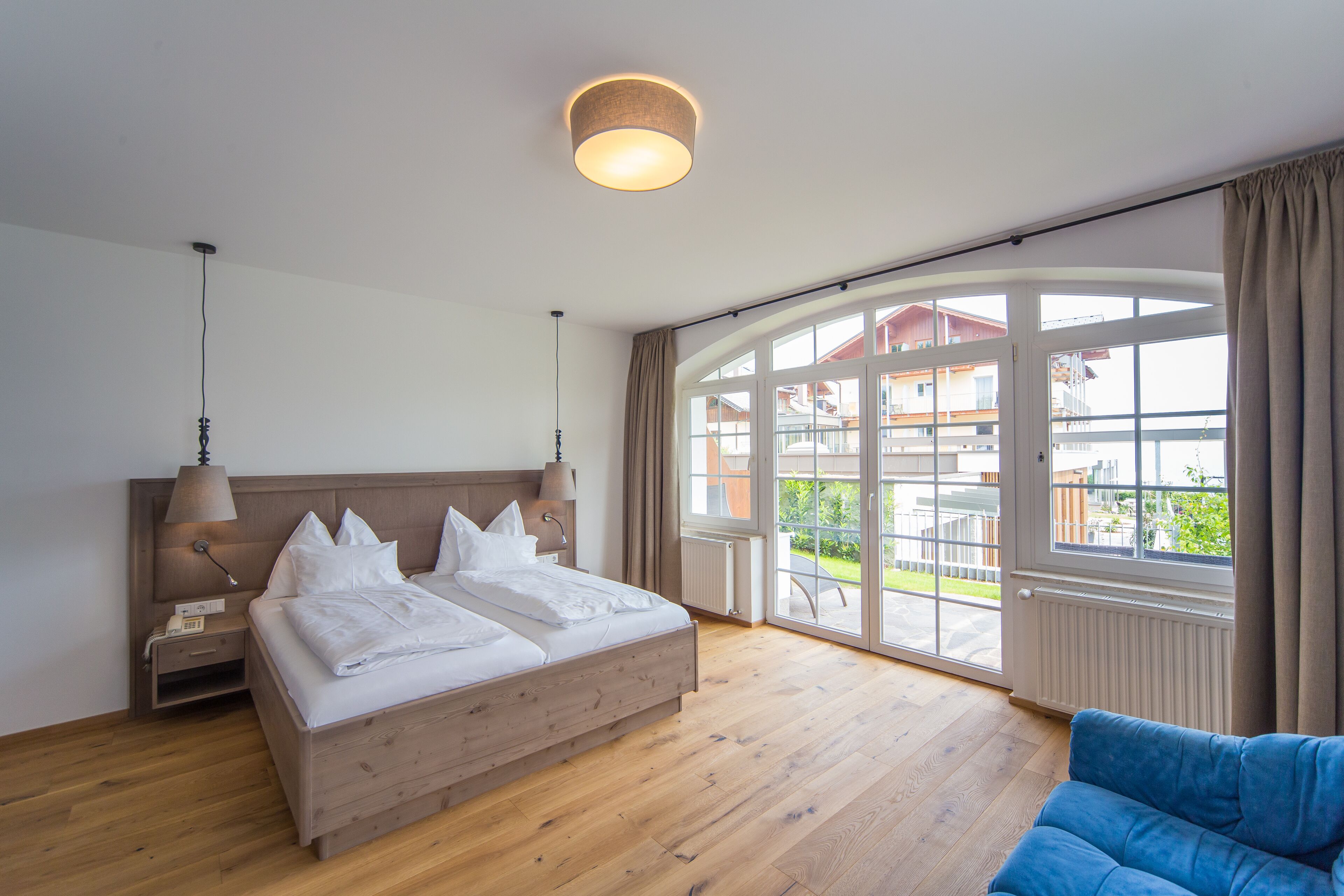 Quarto com uma cama grande, mesa de cabeceira, luminária e vista para o exterior através de uma janela ampla.