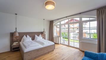Quarto com uma cama grande, mesa de cabeceira, luminária e vista para o exterior através de uma janela ampla.