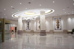 Um hall amplo com pé direito alto, colunas imponentes e luminárias modernas.