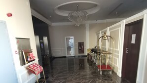 Um hall amplo com piso de mármore, um lustre e um carrinho de bagagem vermelho e dourado.