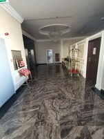 Um hall amplo com piso de mármore, um lustre e um carrinho de bagagem vermelho e dourado.