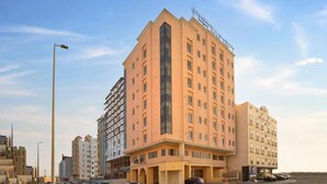 Um hotel com vários andares, um átrio central, diversas varandas e estacionamento.