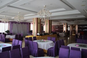 Uma sala de banquetes com mesas redondas e cadeiras roxas, lustres e um palco.