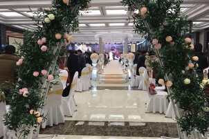 Salão de festas com corredor central, toalhas de mesa brancas e decoração floral.