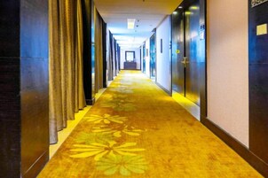 Corredor de hotel com piso carpeteado, portas em ambos os lados e uma fonte de luz ao fundo.