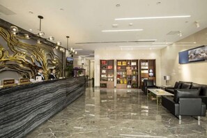 Um saguão de hotel com um balcão de recepção de mármore, uma área de estar com sofás e poltronas, e uma livraria.