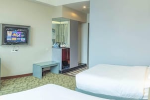 Quarto de hotel com duas camas, uma televisão, uma mesa pequena e um guarda-roupa.