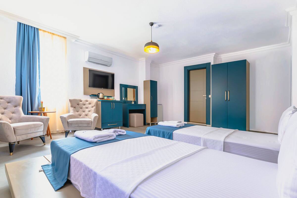 Quarto de hotel com duas camas, uma escrivaninha, uma cadeira, televisão e guarda-roupa.