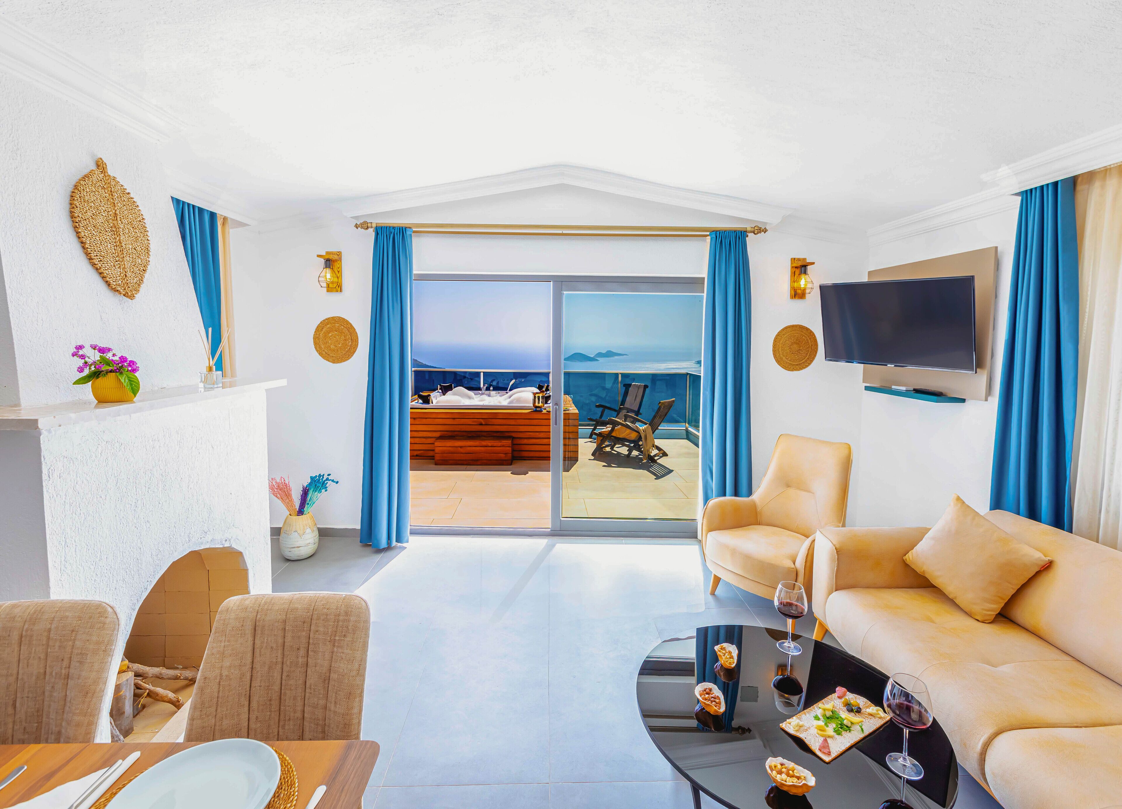 Uma sala de estar moderna com sofá, mesa de jantar e cadeiras, uma varanda com vista para o mar e uma televisão de tela plana fixada na parede.