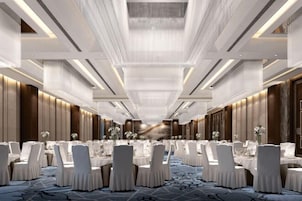 Um amplo salão de banquetes com mesas e cadeiras redondas, teto alto com luminária central e carpete estampado.