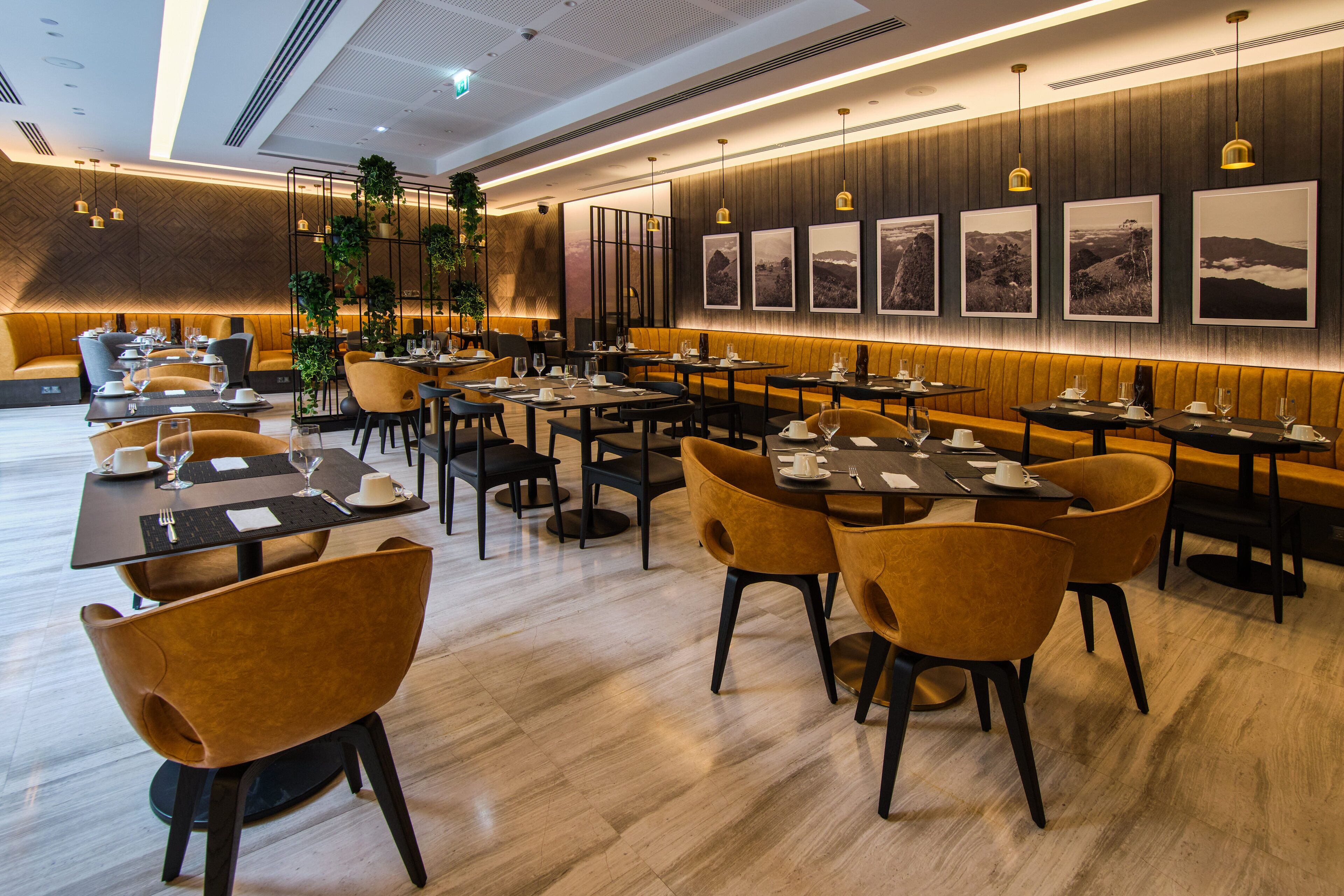 Um restaurante moderno com paredes de painel de madeira, cadeiras pretas e amarelas, e mesas preparadas para refeições.
