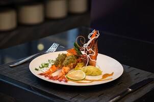Prato de comida com camarões, vegetais e um enfeite sobre uma mesa escura.