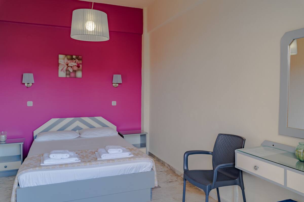 Quarto com cama, mesas de cabeceira, escrivaninha, cadeira, abajur e espelho.