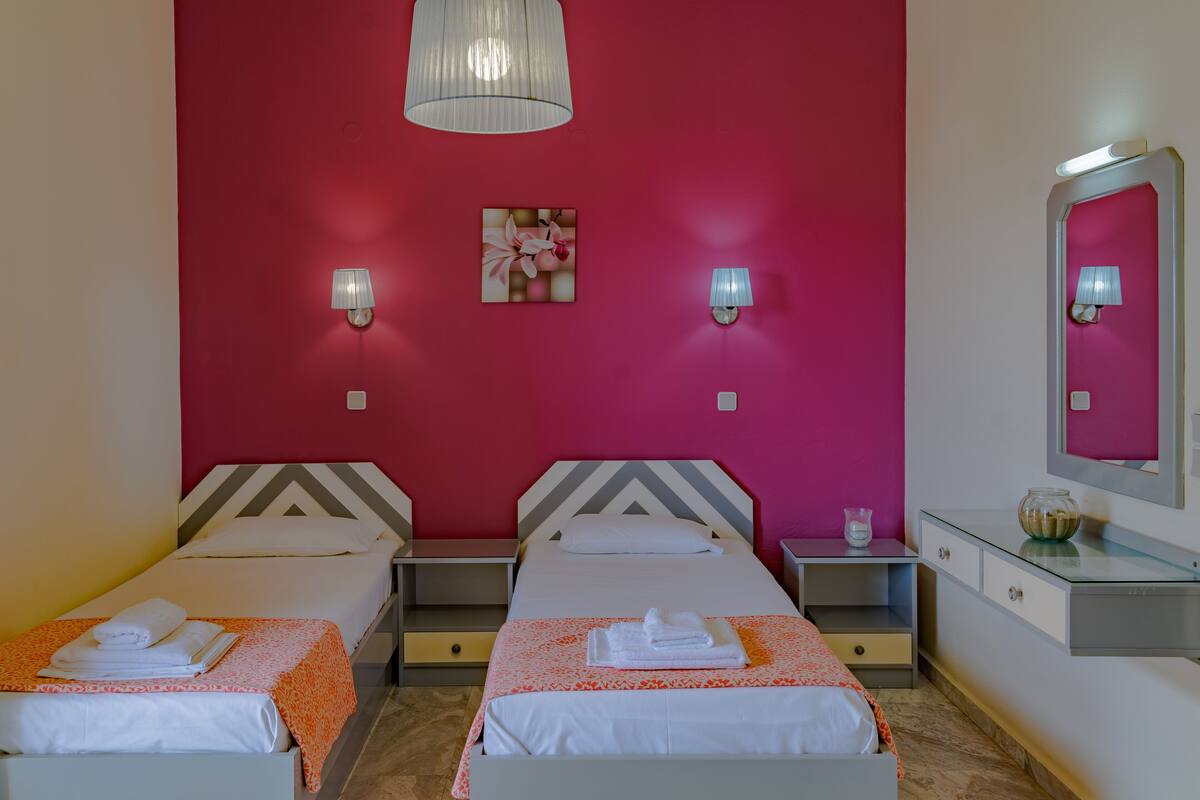 Quarto de hotel com duas camas, um espelho grande e luminárias fixadas na parede.