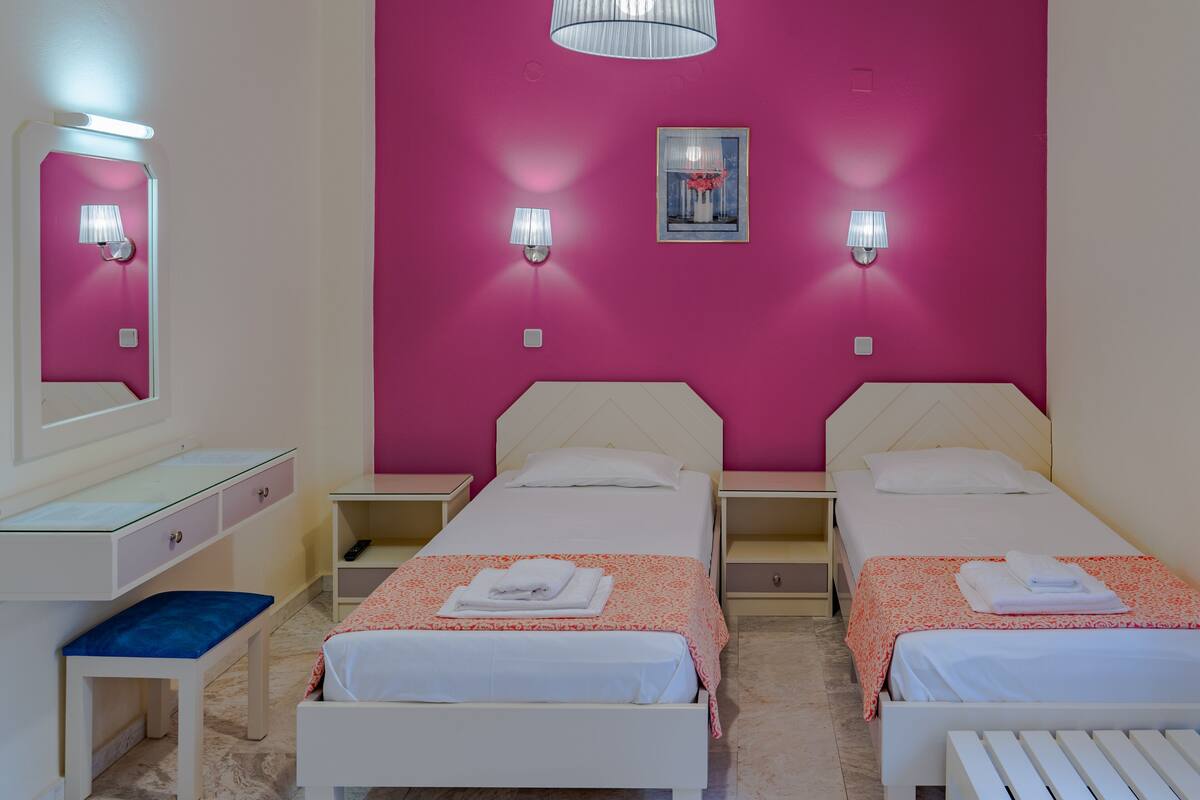 Quarto com duas camas, uma escrivaninha e um espelho.