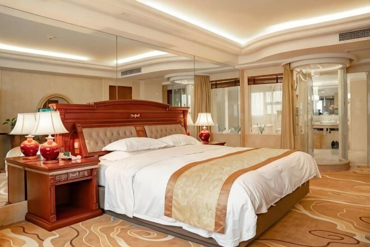 Um quarto de hotel espaçoso com uma cama grande, abajures, mesa de cabeceira e um espelho.