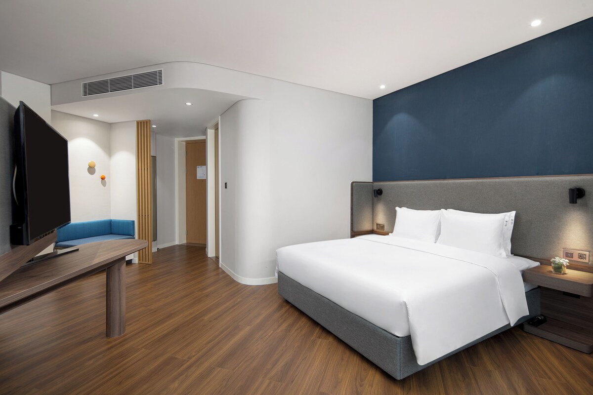 Quarto de hotel moderno com cama, mesas de cabeceira, televisão e um espaço para sentar.