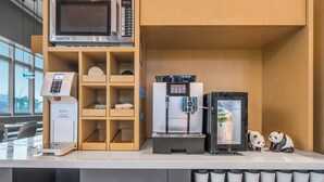 Uma cozinha compacta com micro-ondas, máquina de café, geladeira e um dosador. Há duas figuras de panda no balcão.
