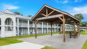 Um motel com área de estar coberta ao ar livre, piscina e um edifício de dois andares com varandas.