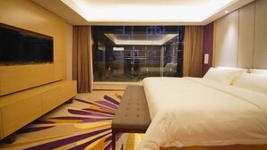 Quarto de hotel moderno com cama grande, TV de tela plana, um banco e porta de vidro que dá para uma varanda.